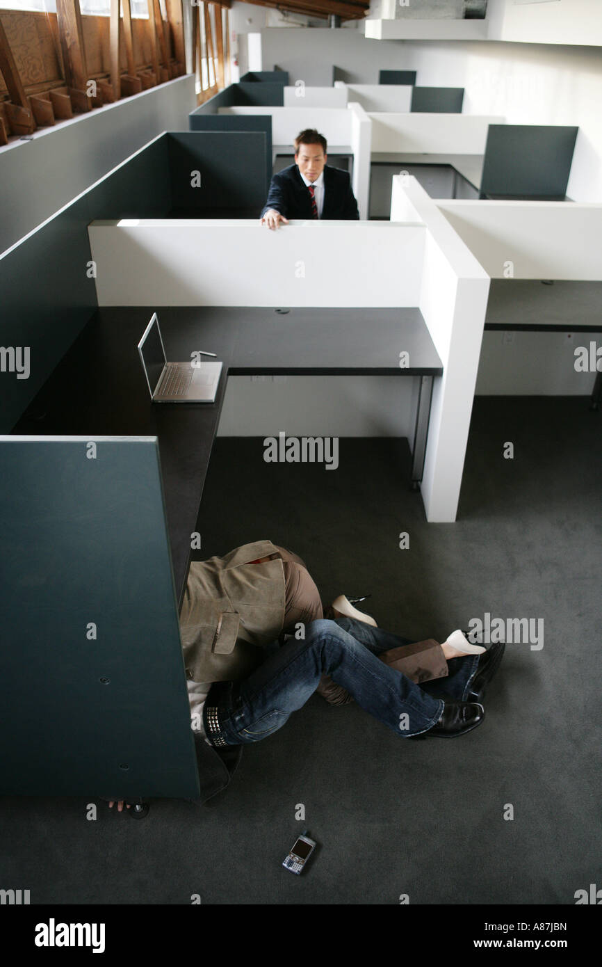 Man looking at a couple under a desk in the office Stock Photo - Alamy
